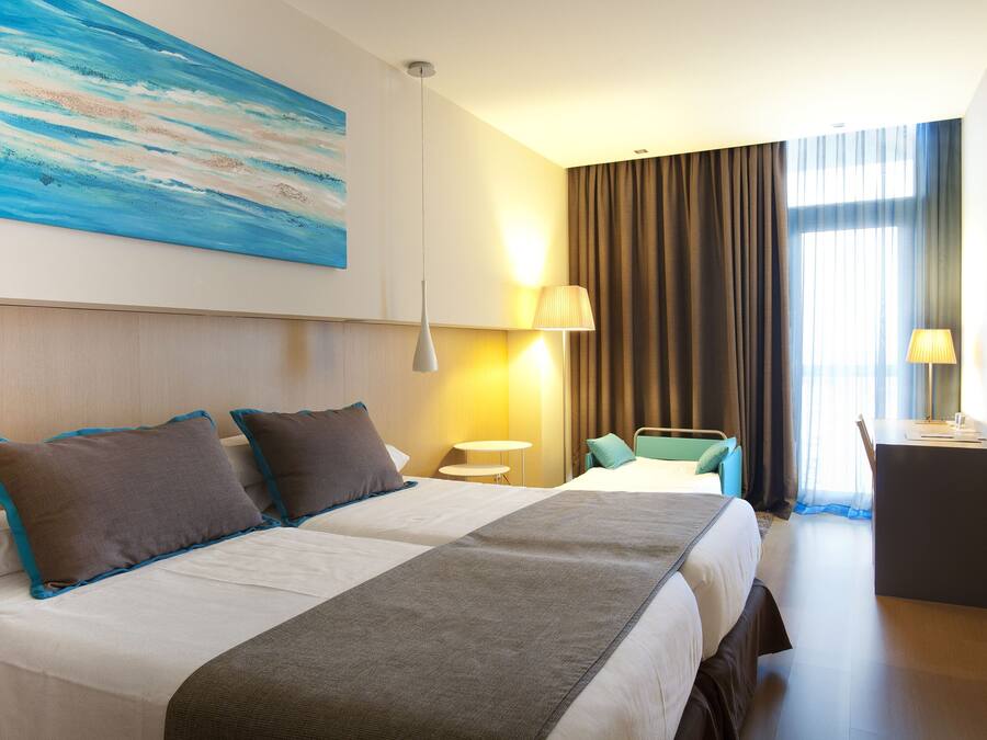Quarto de hotel com duas camas, uma escrivaninha, uma cadeira, um abajur e um quadro na parede.