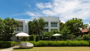 Hotel moderno com estrutura em dois andares, cercado por vegetação exuberante e céu azul límpido.