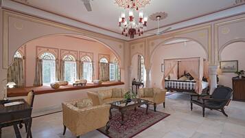 Uma sala de estar ampla com teto alto, lustres ornamentados e uma grande janela com vitrais.