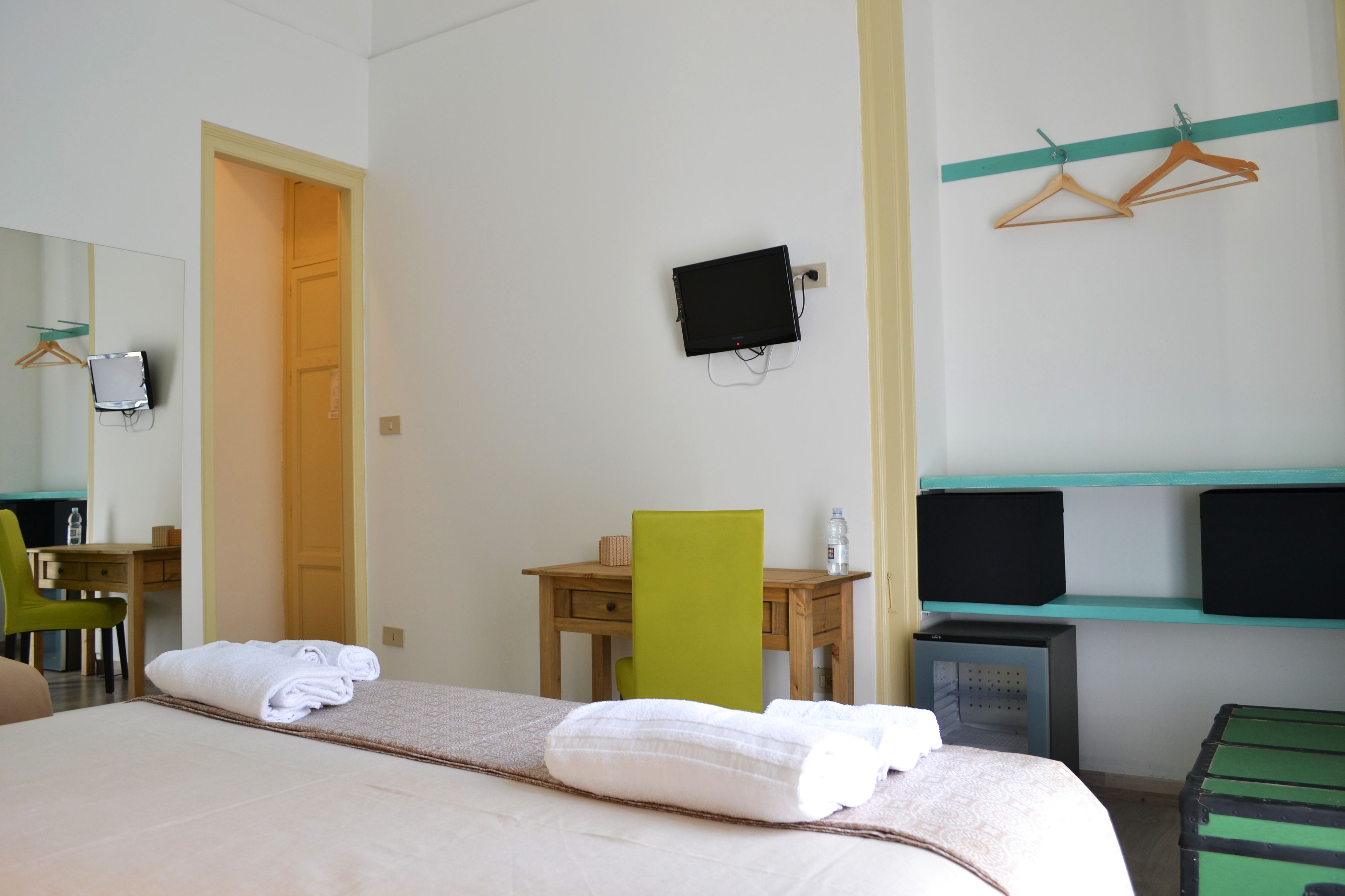 Quarto de hotel com cama, escrivaninha, cadeira, televisão fixada na parede e guarda-roupa.