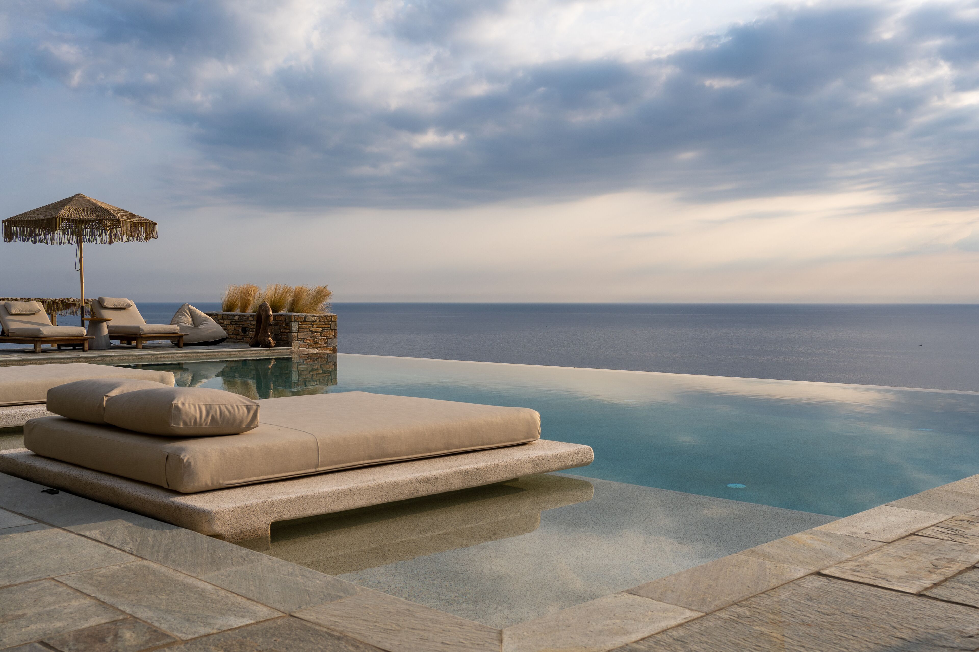 Uma piscina infinita com espreguiçadeiras e um guarda-sol, com vista para o mar.