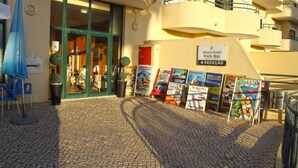 Entrada de hotel com placa para AtlanticHotels Plaza Real, área de estar externa e calçada de pedra.