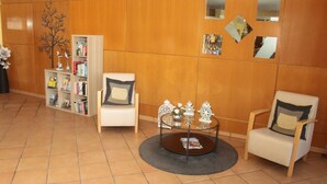 Um lobby acolhedor com parede de madeira, uma estante de livros, duas poltronas, uma mesa de centro e objetos decorativos.