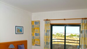 Quarto de hotel com duas camas, uma mesa, uma cadeira, um telefone, uma luminária e vista para a paisagem pela janela.