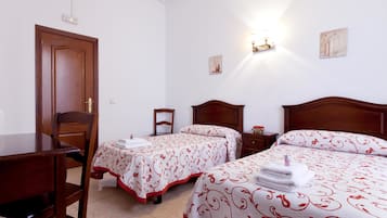 Quarto de hotel com duas camas de solteiro, uma escrivaninha de madeira, uma cadeira e uma mesa de cabeceira com um vaso de flores.