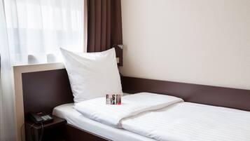 Quarto de hotel com uma cama de solteiro, telefone ao lado da cama e janela com cortinas.
