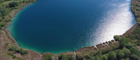 Vista aérea de um lago grande e irregular, cercado por vegetação densa e algumas trilhas.