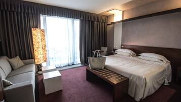Quarto de hotel com cama, sofá, escrivaninha e luminária.