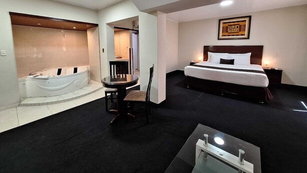 Quarto de hotel com cama, escrivaninha, poltrona, banheira e um quadro na parede.