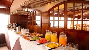 Buffet com diversos alimentos e bebidas, incluindo frutas, doces e sucos.