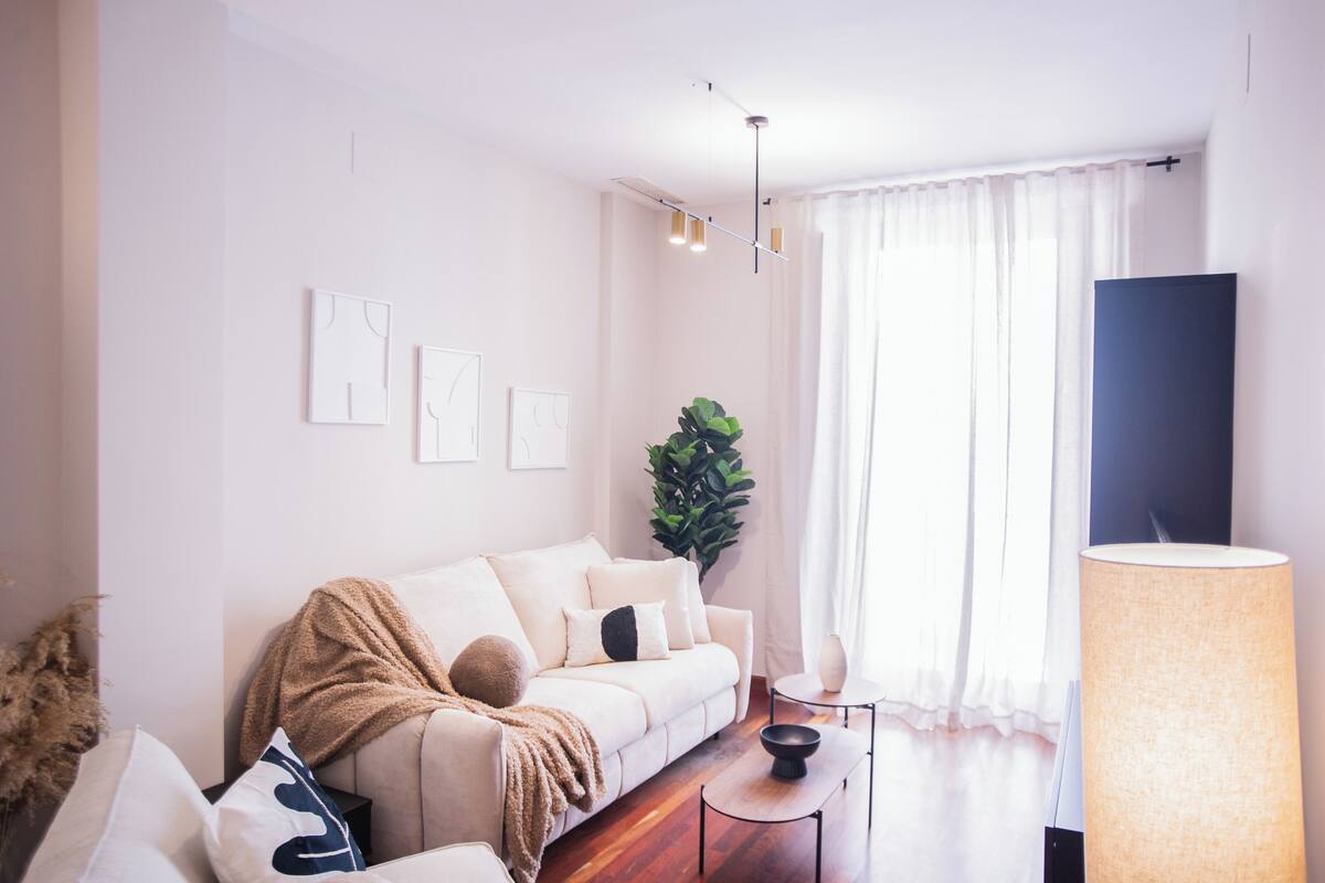 Uma sala de estar moderna com um sofá, uma mesa de centro, um abajur e uma janela grande com cortinas.