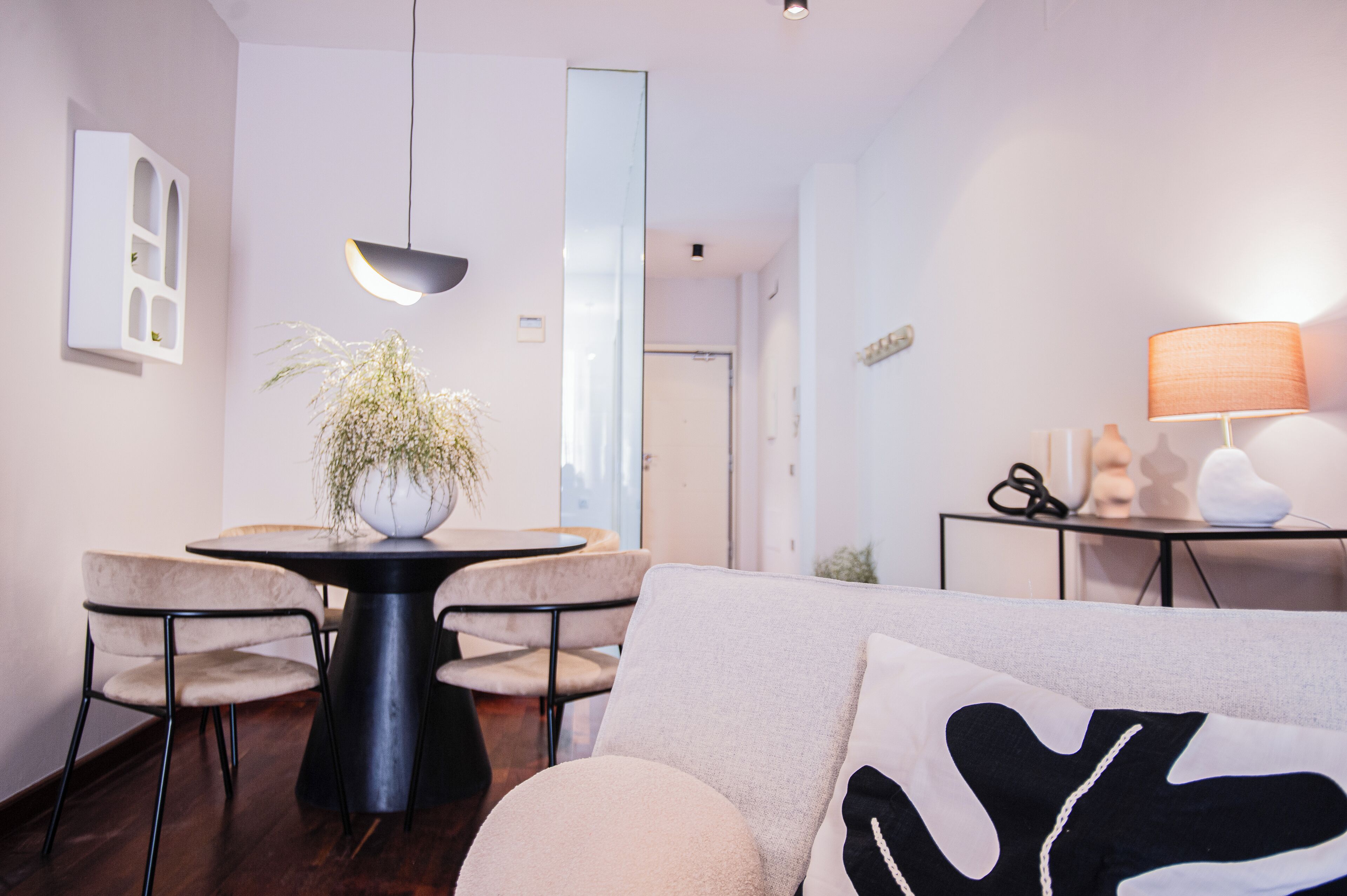 Uma sala de jantar moderna com uma mesa redonda, quatro cadeiras, um lustre e um vaso com planta.
