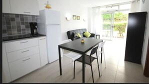 Uma cozinha compacta com armários brancos, bancada preta e uma área de refeições com mesa preta e cadeiras brancas.