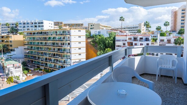 Varanda com mesa e cadeiras, com vista para um horizonte urbano com edifícios e palmeiras.