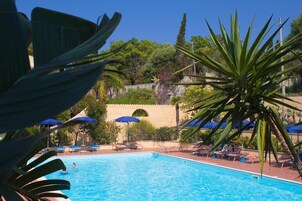 Piscina com espreguiçadeiras e guarda-sóis, cercada por vegetação e um muro de pedra.