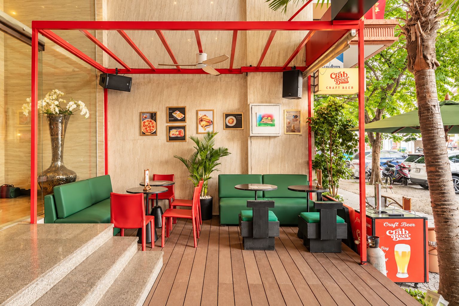 Uma área externa com sofás verdes e cadeiras vermelhas, piso de madeira e um letreiro de Cerveja Artesanal.