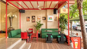 Uma área externa com sofás verdes e cadeiras vermelhas, piso de madeira e um letreiro de Cerveja Artesanal.