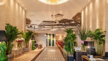 Um saguão de hotel com um corredor central, um balcão de recepção e um mural na parede.