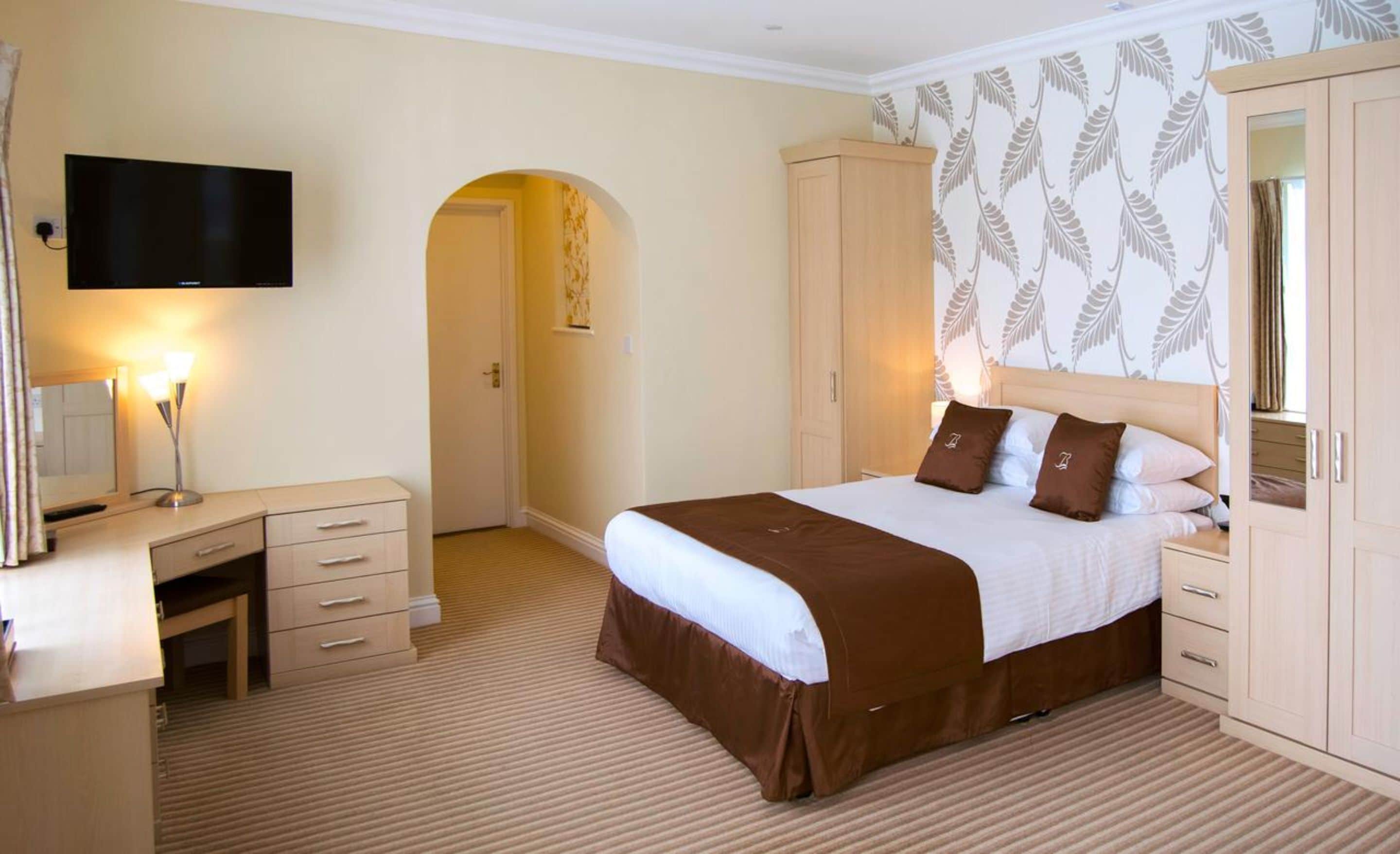 Quarto de hotel com cama, escrivaninha, televisão e guarda-roupa.