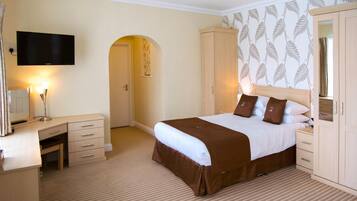 Quarto de hotel com cama, escrivaninha, televisão e guarda-roupa.