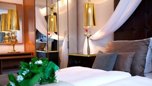 Quarto de hotel com cama, mesa de cabeceira, luminária, espelho e cortinas com drapeado.