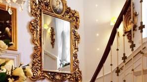 Uma escadaria imponente com grades douradas ornamentadas e um espelho com moldura elaborada.