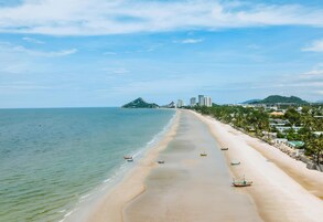 Uma praia extensa com barcos, céu claro e edifícios ao longe.