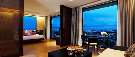 Quarto de hotel moderno com uma varanda espaçosa, uma cama, uma mesa de jantar com um vaso de flores e vista para a paisagem urbana.