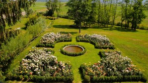 Um jardim bem cuidado com um lago circular, rodeado por canteiros de flores e árvores.
