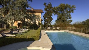 Piscina com espreguiçadeiras e um edifício ao fundo.