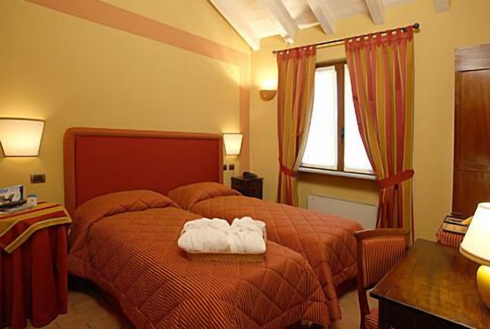 Quarto de hotel com uma cama grande, duas mesas de cabeceira, uma luminária na mesa de cabeceira e uma janela com cortinas.