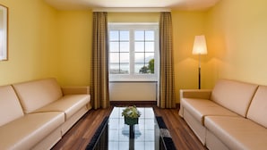 Quarto com dois sofás bege, uma mesa de centro de vidro com uma planta, um abajur e uma janela com cortinas.