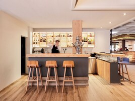 Uma área de bar com balcão de madeira, banquetas e prateleiras cheias de garrafas.