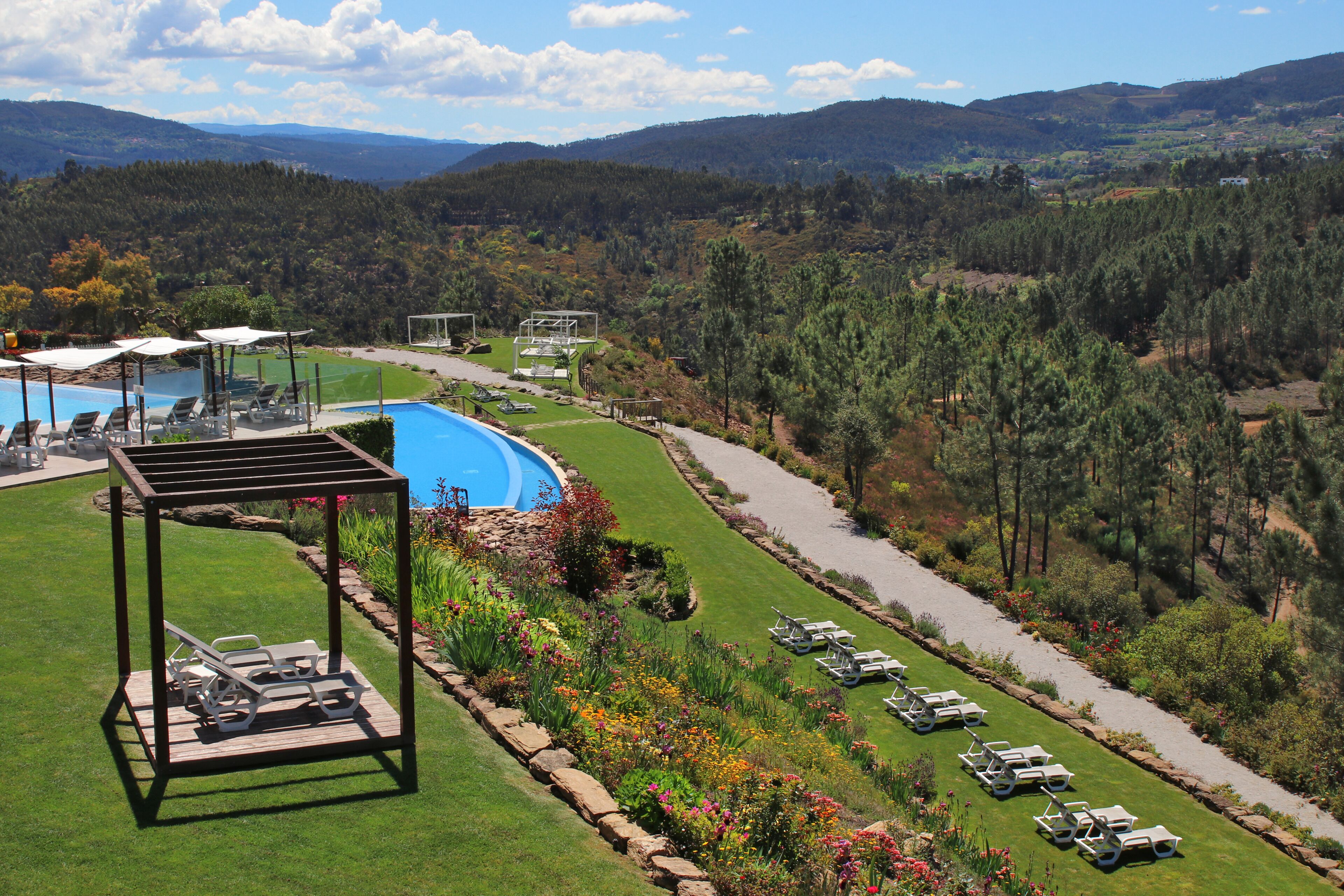 Uma área de piscina com espreguiçadeiras e um pérgola, cercada por um gramado bem cuidado e vista para as colinas ao redor.
