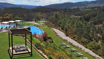Uma área de piscina com espreguiçadeiras e um pérgola, cercada por um gramado bem cuidado e vista para as colinas ao redor.
