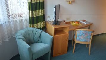 Quarto com escrivaninha, cadeira, laptop, luminária e pequena mesa com uma tábua de frutas.