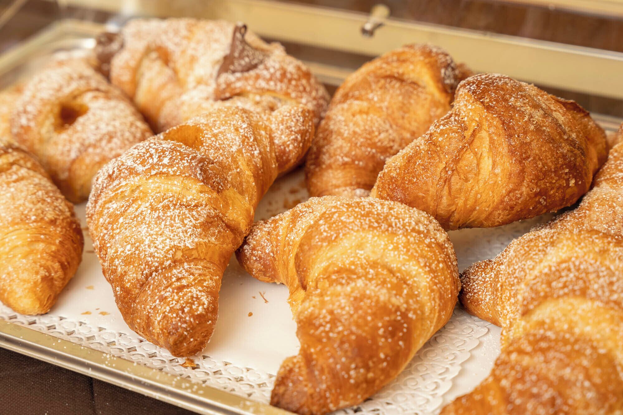 Uma bandeja com diversos doces, incluindo croissants e um éclair de chocolate, polvilhada com açúcar de confeiteiro.
