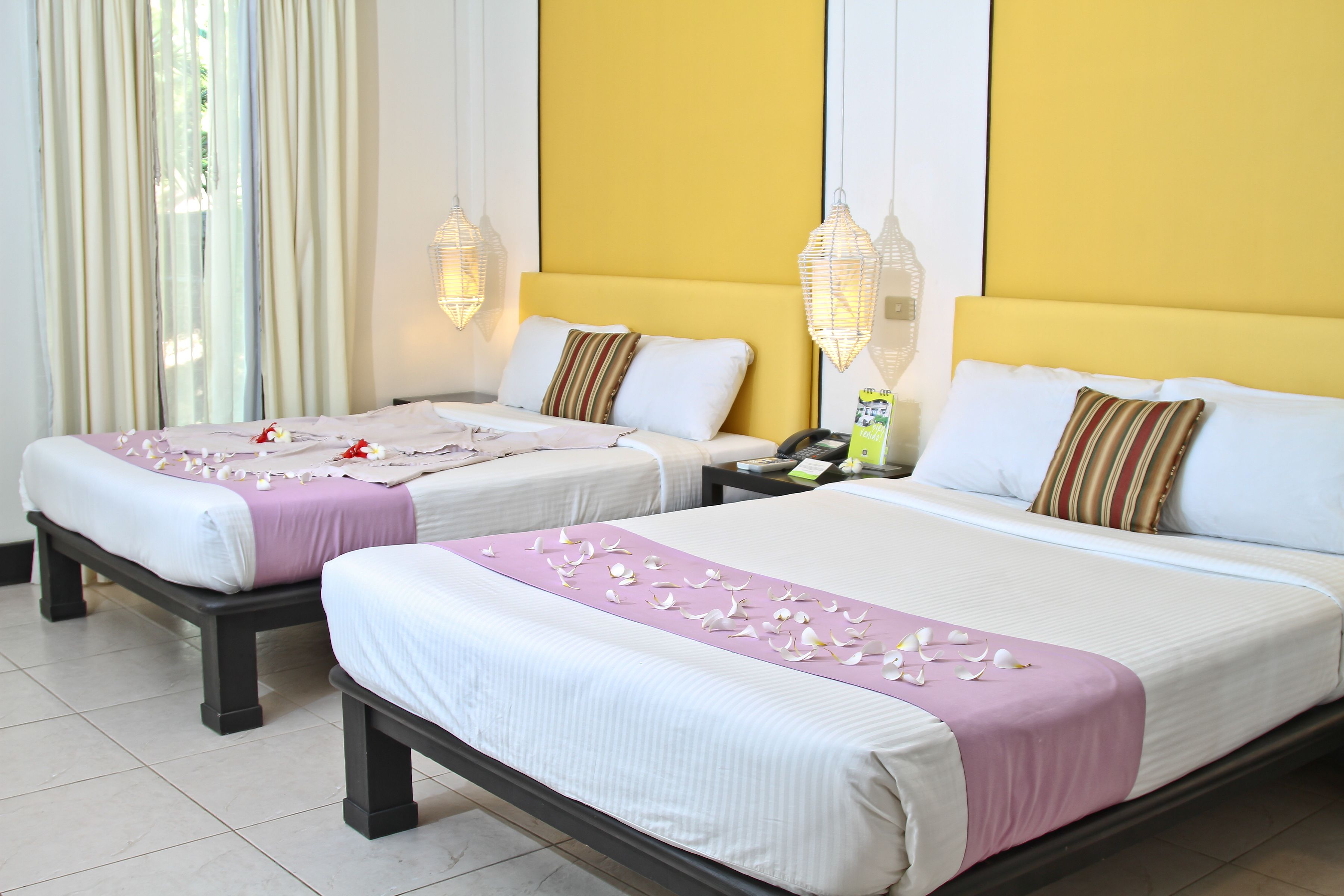 Duas camas de casal com lençóis brancos, colchas rosa e pétalas de flores decorativas.