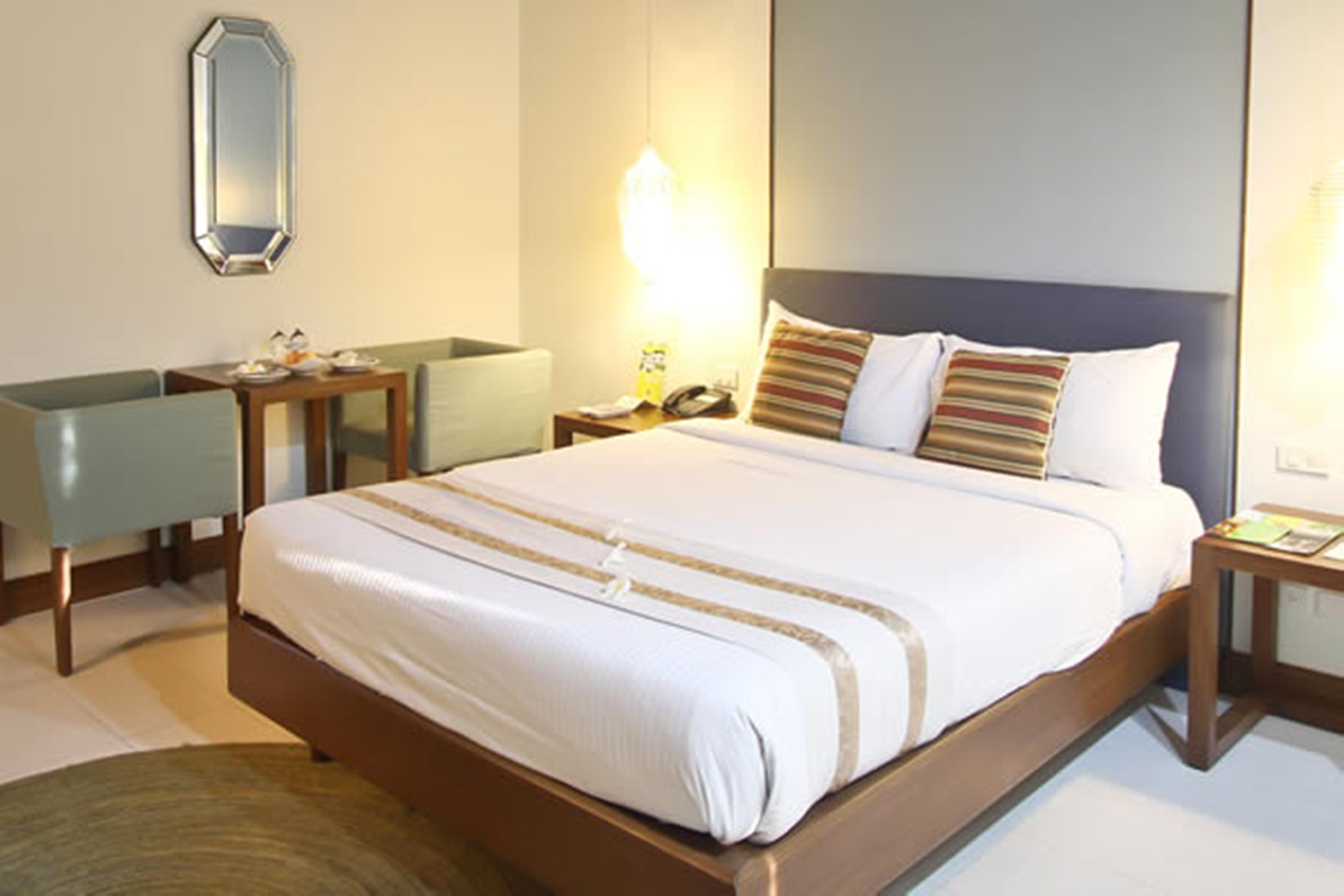 Quarto de hotel com uma cama grande, uma mesa de cabeceira, uma cadeira e um espelho na parede.