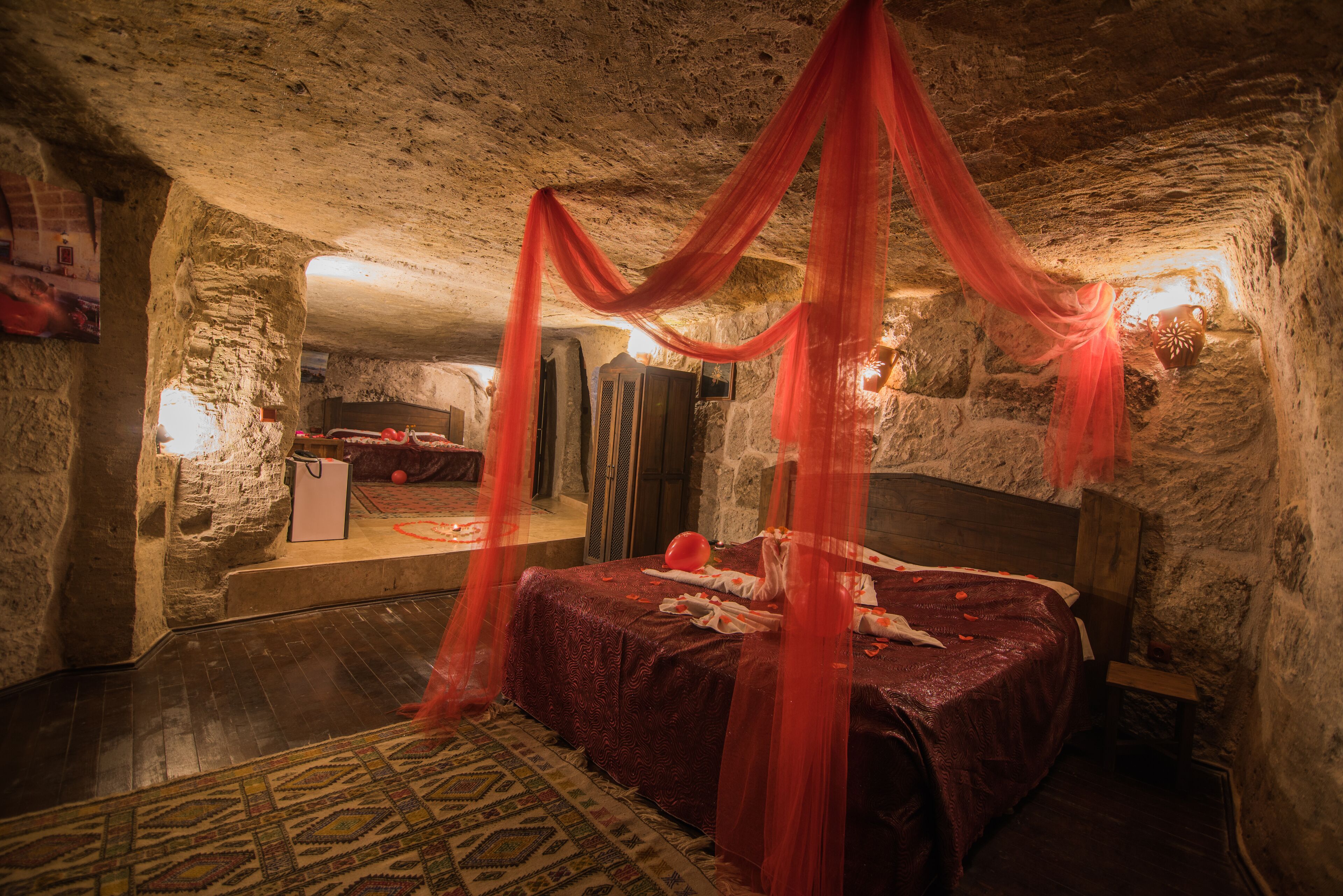 Quarto com paredes de pedra, uma cama, um dossel vermelho e um tapete estampado.
