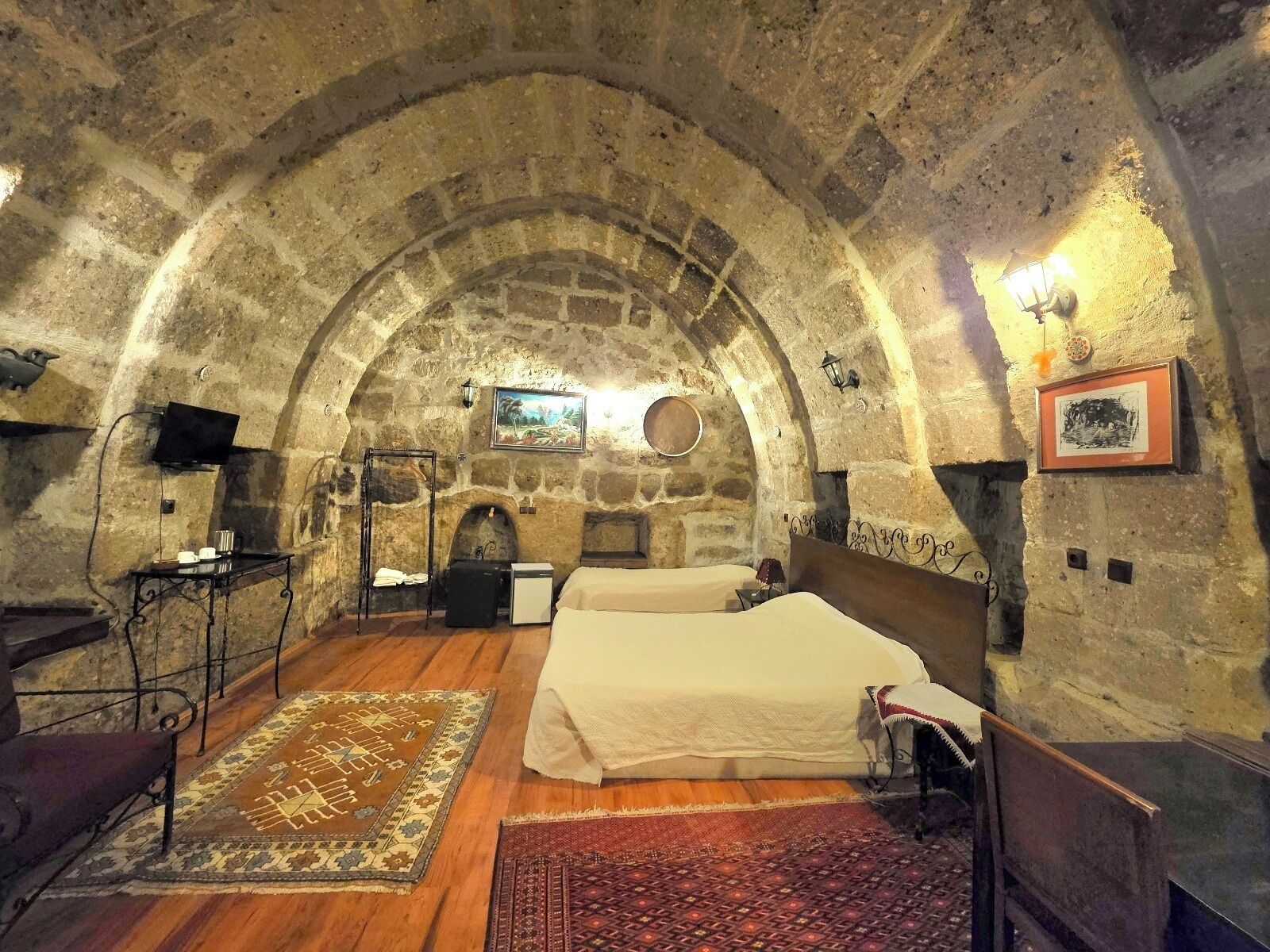 Quarto com paredes de pedra, uma cama, uma mesinha, uma televisão e uma lareira.