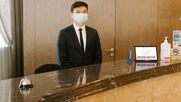 Balcão de recepção de hotel com um homem de terno, painéis de madeira, relógios e um laptop.