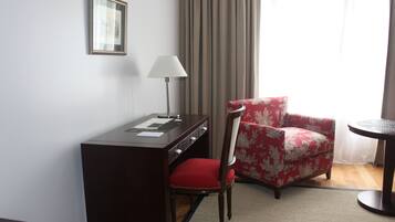 Quarto de hotel com escrivaninha, cadeira, luminária e uma mesa redonda.