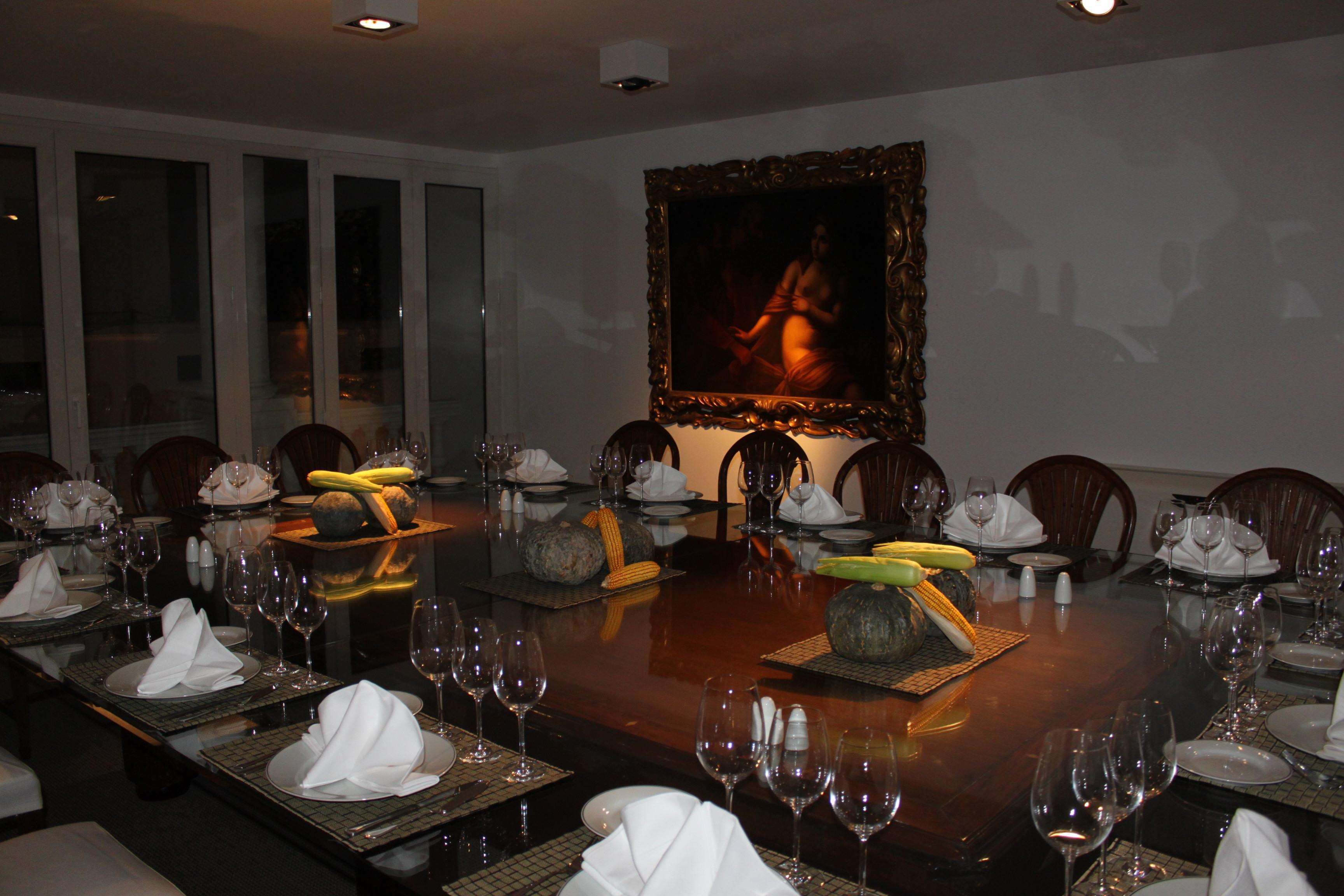Uma sala de jantar formal com uma longa mesa posta para refeição, cadeiras e um grande quadro emoldurado na parede.