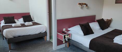 Quarto de hotel com duas camas, cabeceira vermelha, mesa de cabeceira pequena com telefone e abajur, e piso coberto por carpete.