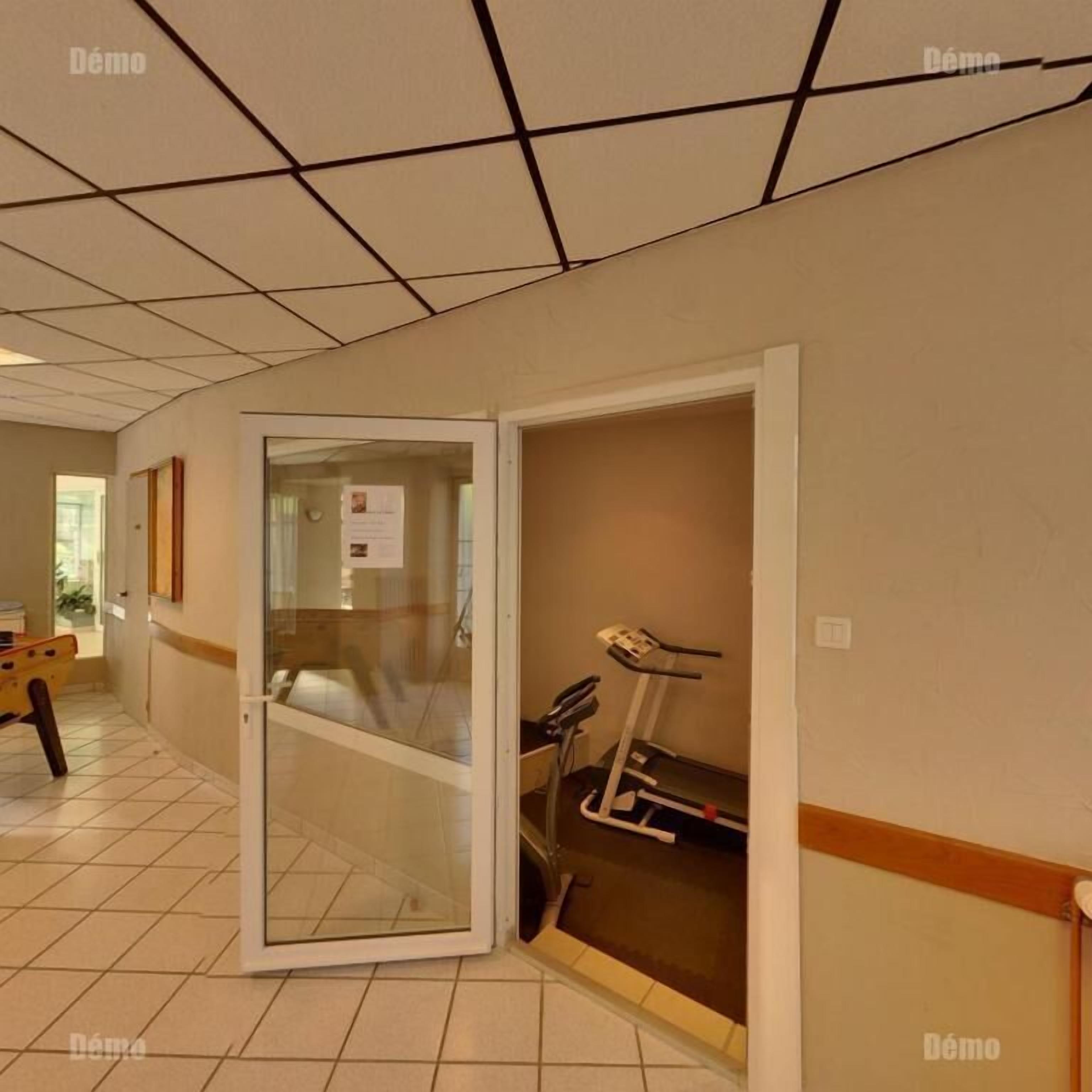 Um corredor com uma porta de vidro que dá para um quarto com esteira.