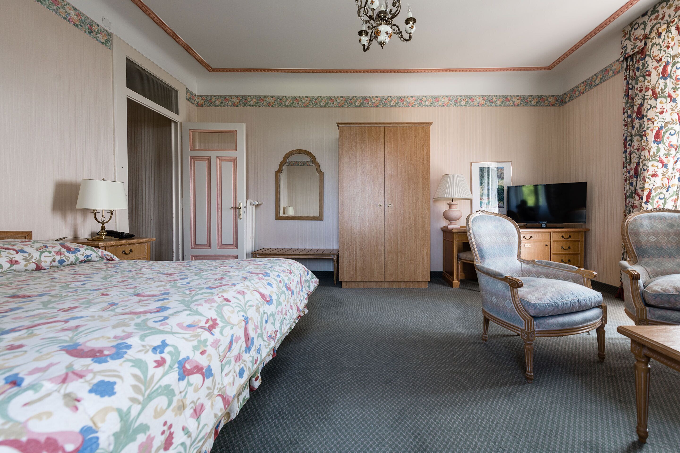 Quarto de hotel com cama, uma cadeira, televisão e guarda-roupa.