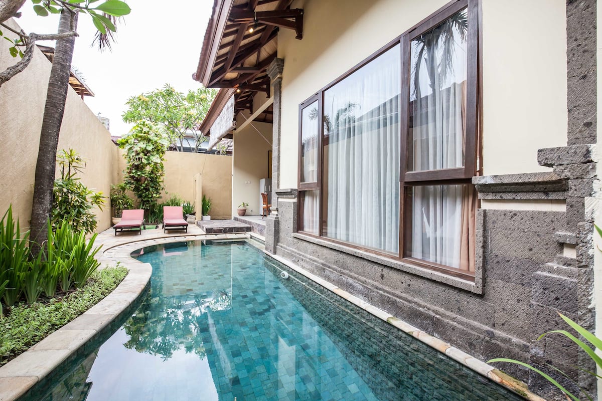 Piscina com borda azulejada, rodeada por um muro de pedra e uma pérgula de madeira.
