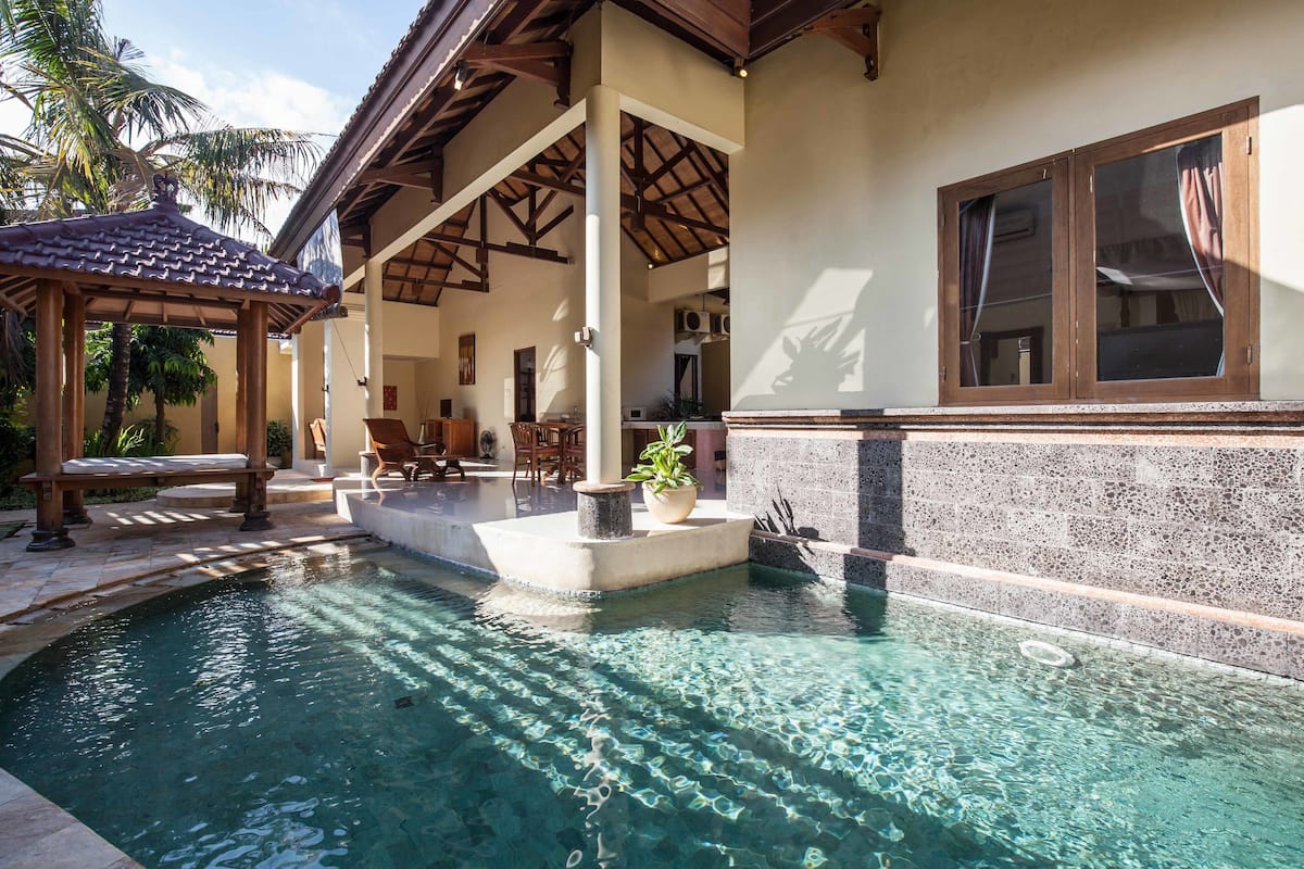 Área de piscina com pergolado, assentos e muro de pedra.