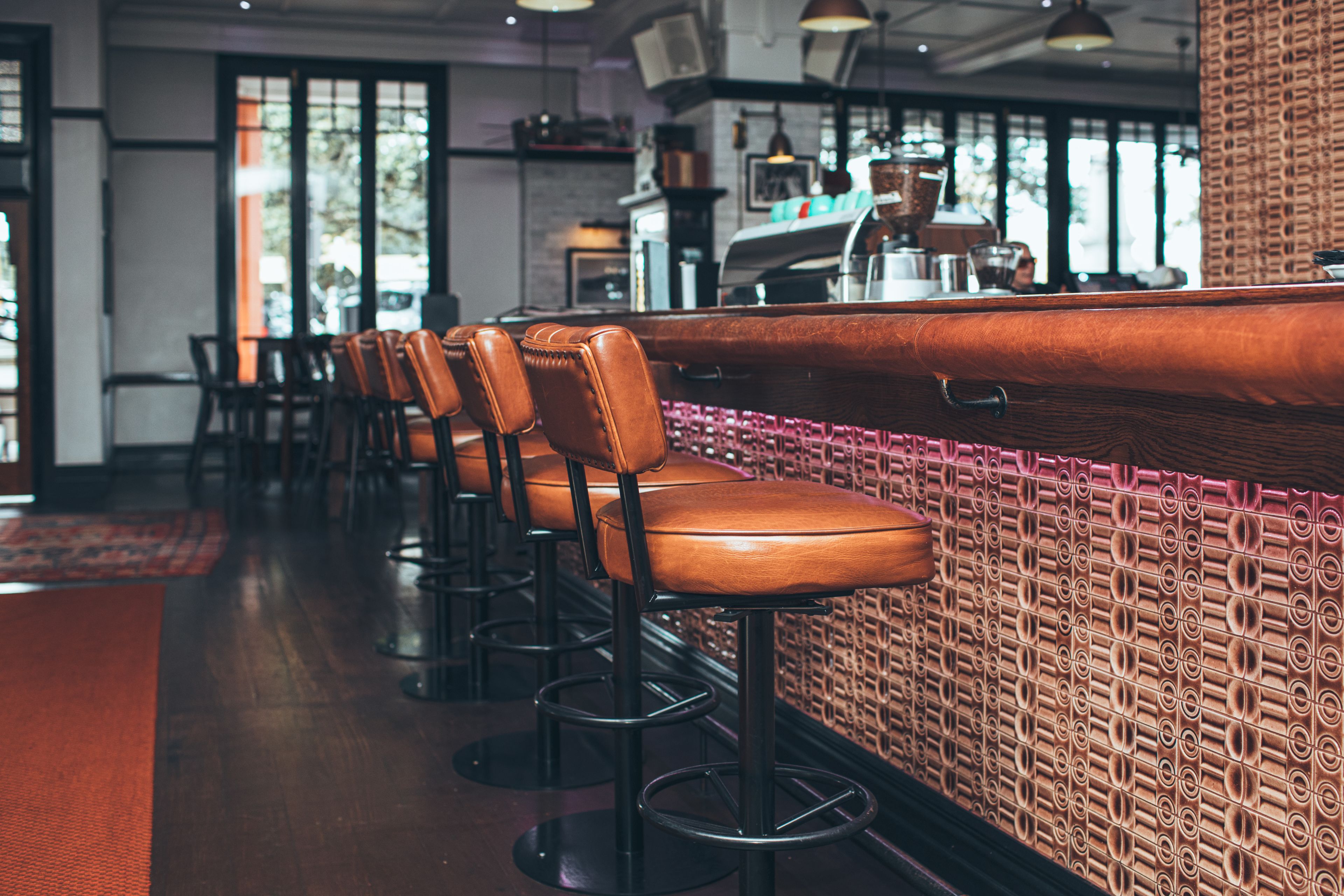Uma área de bar com banquetas de couro e um painel trançado.